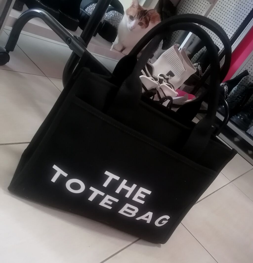 Crna platnena torba sa ručkama i natpisom "THE TOTE BAG". Ima