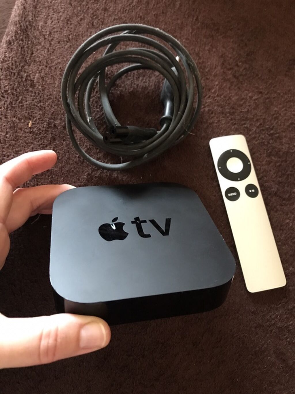 Apple TV (set‑top box) sa daljinskim upravljačem i napojnim kablom. -