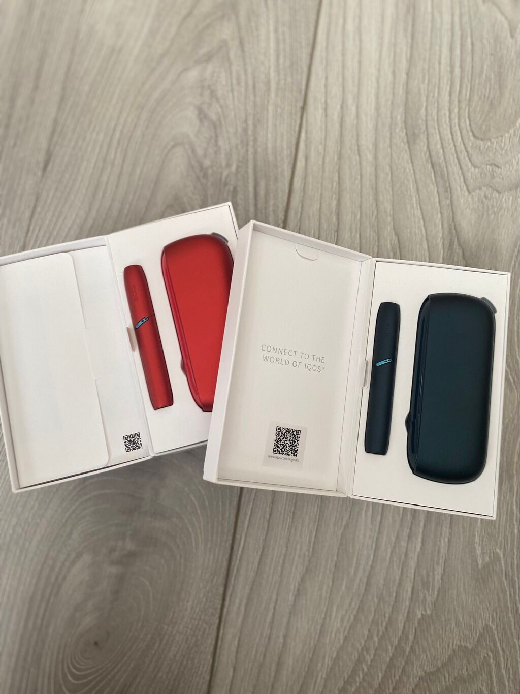 Dva IQOS-a, crveni i crni, uz njih punjači i čistači, u ispravnom