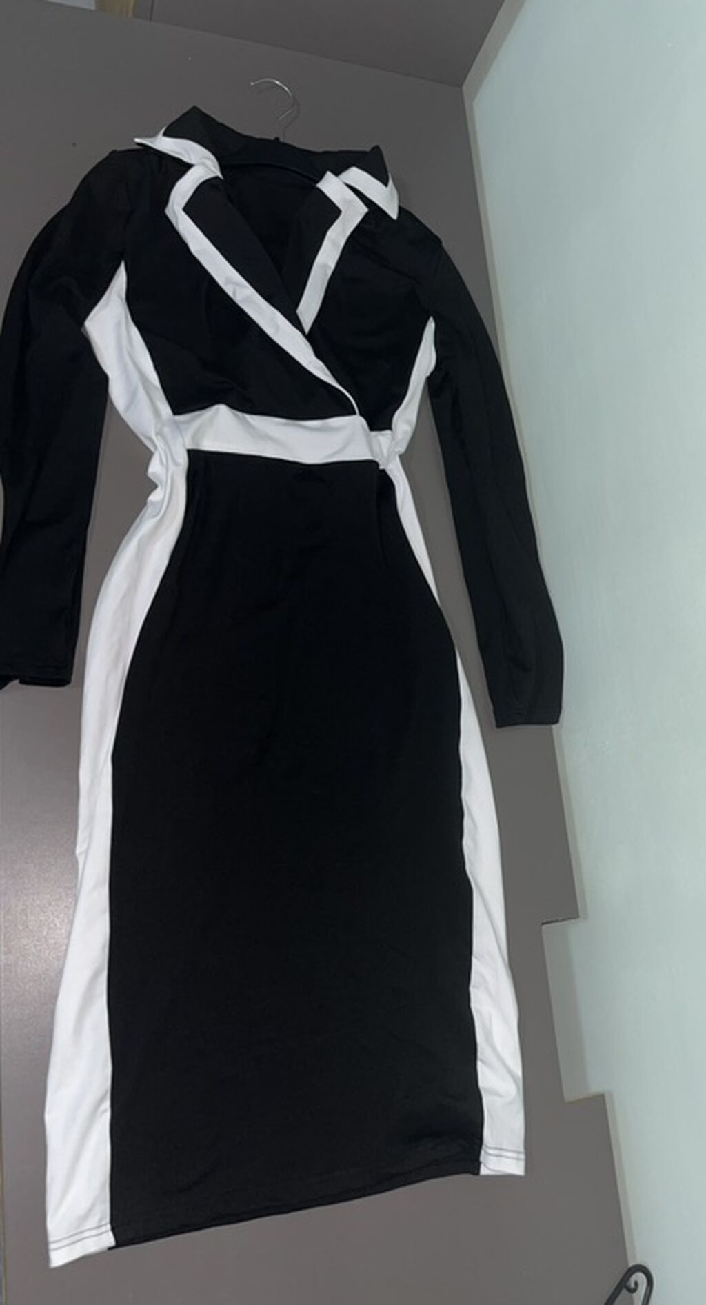 Elegantna crno-bela haljina midi dužine sa dugim rukavima. Model je u