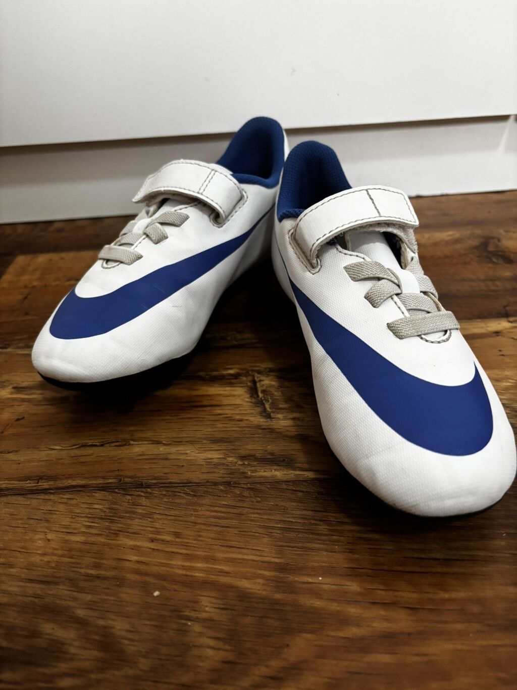 Dečje fudbalske kopačke Nike – bela osnova sa plavim Swoosh logom. -